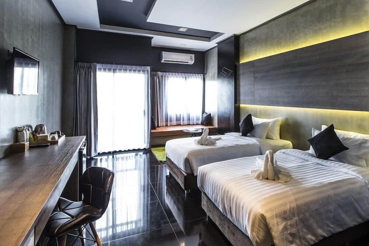 Quarto de hotel com escrivaninha, duas camas, um sofá e vista para o exterior.