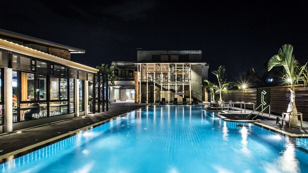 Uma piscina com design moderno, cercada por edifícios com grandes janelas e áreas de estar ao ar livre.