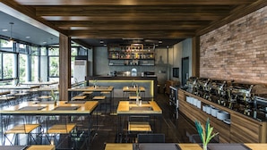 Um restaurante moderno com mesas e cadeiras de madeira, um espaço de bar com prateleiras cheias de garrafas e uma parede de tijolos.