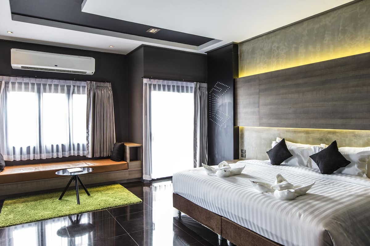 Quarto de hotel moderno com uma cama grande, um espaço de estar com uma pequena mesa e um aparelho de ar condicionado.