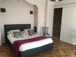 Quarto com cama, almofadas, uma cadeira, uma porta e piso revestido de azulejos.