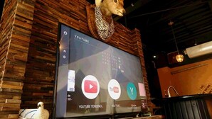 Interface de um canal do YouTube visível numa tela fixada em uma parede de madeira.