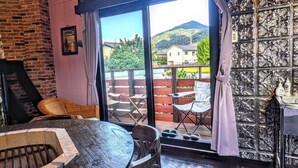 Varanda com móveis de vime, uma mesa e vista para montanhas e casas.