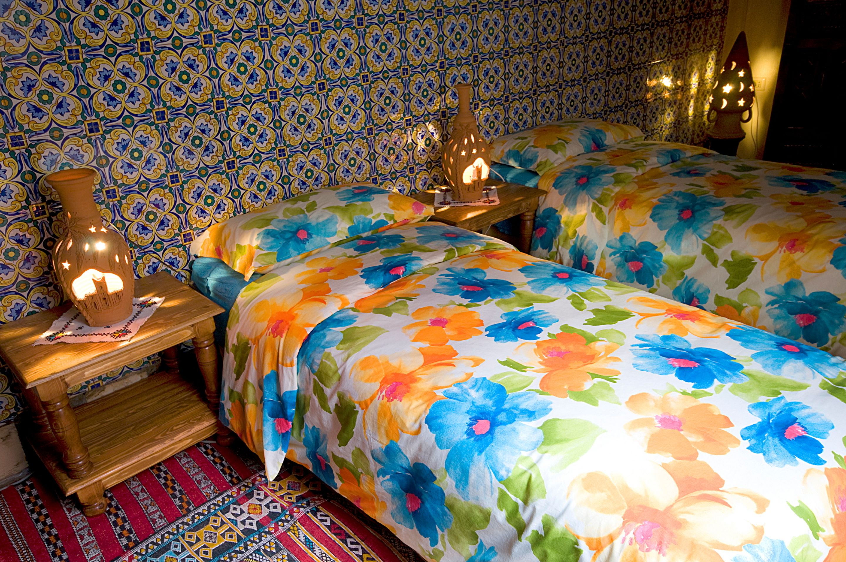 Quarto com duas camas, papel de parede estampado e um vaso decorativo na mesa de cabeceira.