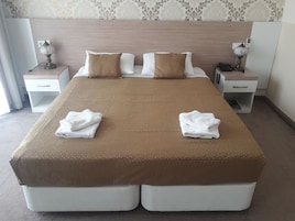 Quarto de hotel com uma cama grande, duas mesas de cabeceira, uma luminária e um telefone.