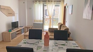 Uma área de refeições com mesa posta para quatro pessoas, um sofá, uma TV e uma pequena mesa com um laptop.