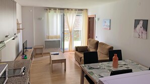 Uma sala de estar moderna com sofá, uma mesa de jantar posta para dois e uma cozinha com fogão e micro-ondas.