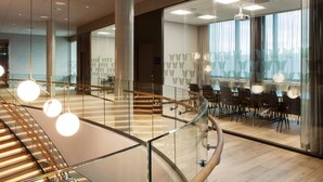 Uma sala de conferências moderna com paredes de vidro, escada de madeira e projetor no teto.