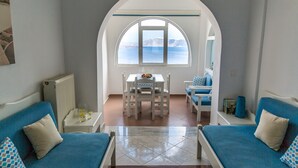 Quarto com vista para o mar, uma mesa de jantar com cadeiras e dois sofás azuis.