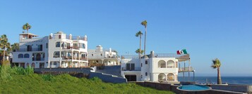 Um edifício branco de vários andares com varandas, piscina e vista para o oceano.
