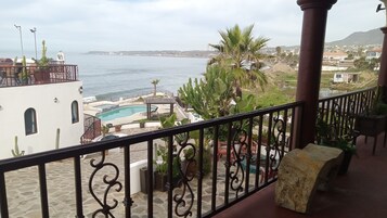 Uma varanda com piso de pedra, piscina e vista para o mar e edifícios ao longe.