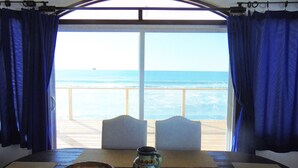 Quarto com vista para o oceano através de uma grande janela, uma mesa com duas cadeiras e um vaso decorativo.