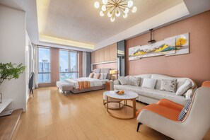 Quarto de hotel moderno com uma cama grande, um sofá, uma mesa de centro e vista para a paisagem urbana através de grandes janelas.