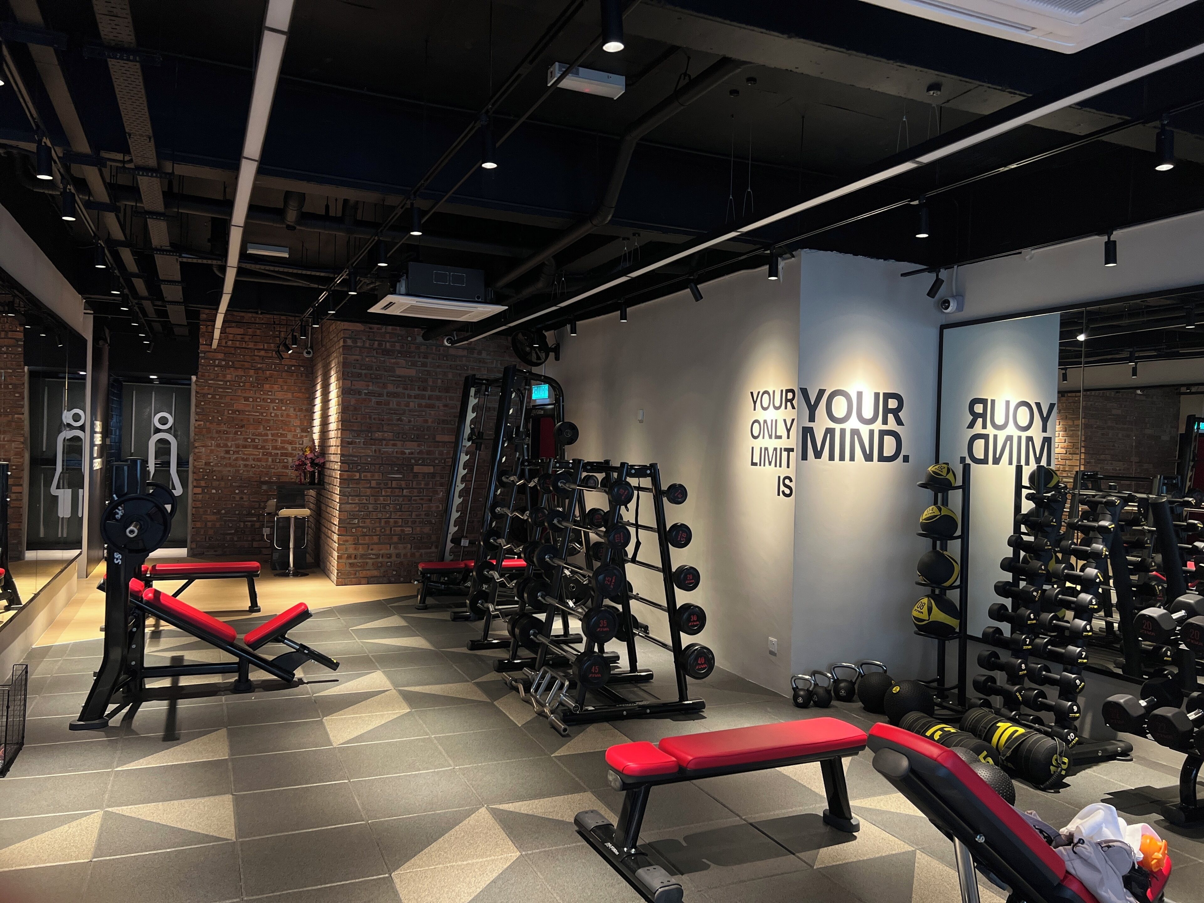 Uma academia com equipamentos de musculação, bancos e frases motivacionais na parede.
