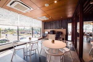 Um interior de cafeteria moderna com mesas redondas e cadeiras brancas, teto de madeira e um quadro de menu na parede.