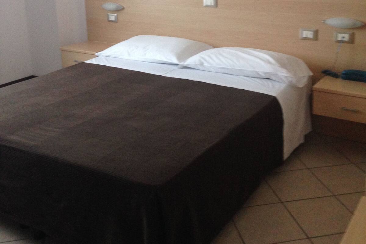 Quarto de hotel com cama, mesa de cabeceira, luminária na parede e parede listrada.