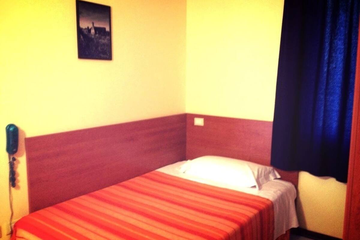 Uma cama de solteiro com colcha listrada em quarto com paredes amarelas e cabeceira escura.