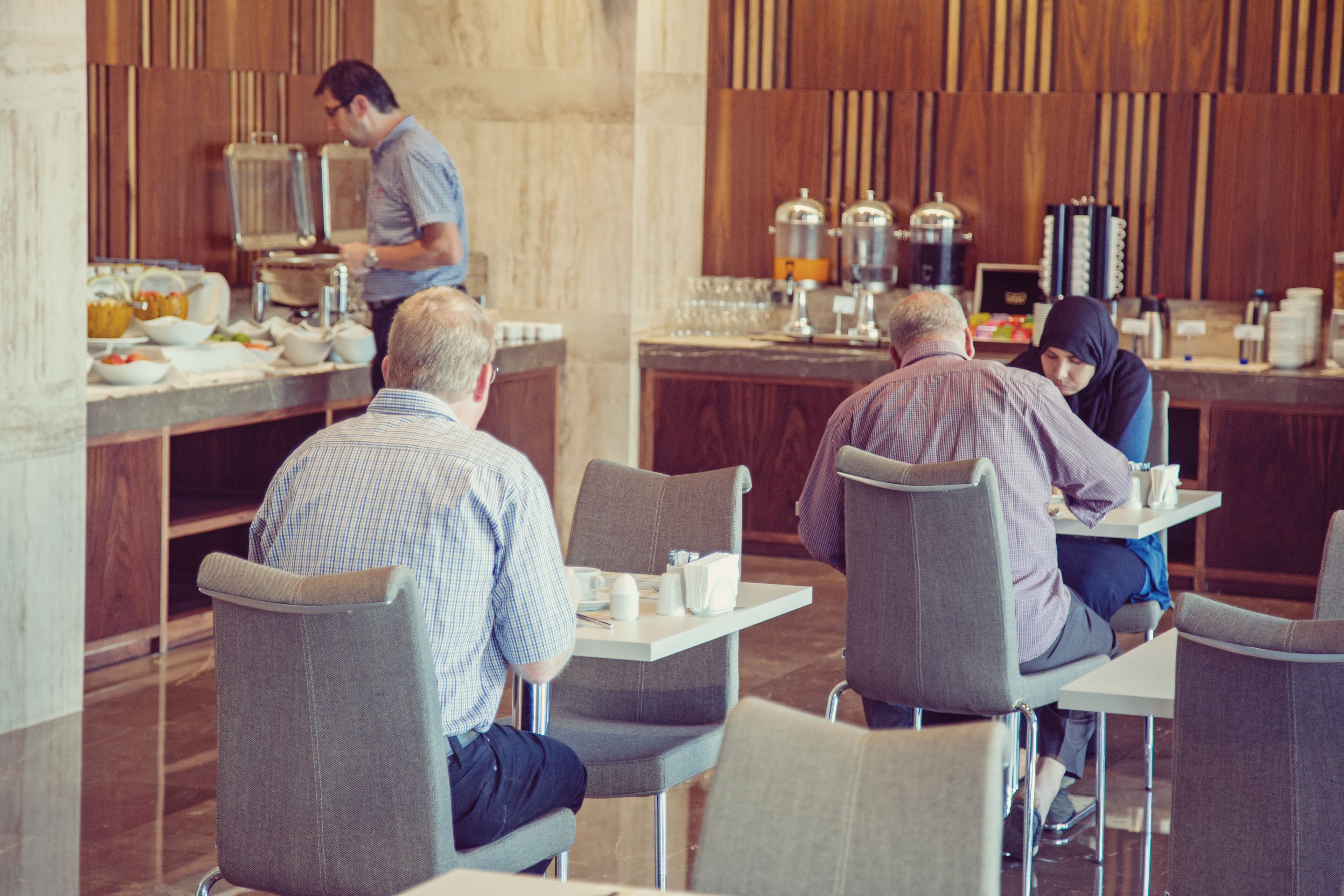Um restaurante com serviço de buffet, incluindo um balcão com comida e bebidas, e vários clientes sentados.