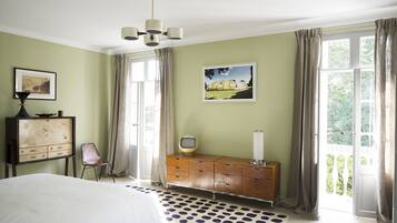 Quarto com cama, cômoda, cadeira, quadro na parede e janela com cortinas.