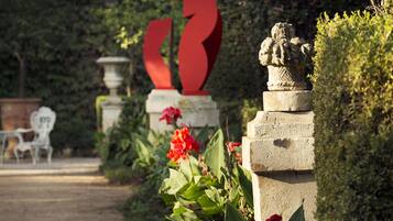 Uma trilha no jardim com uma estátua de pedra, esculturas abstratas vermelhas e flores vermelhas.
