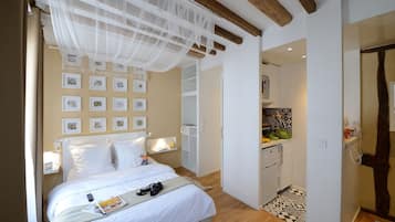 Quarto com cama, mesa de cabeceira e uma pequena cozinha.