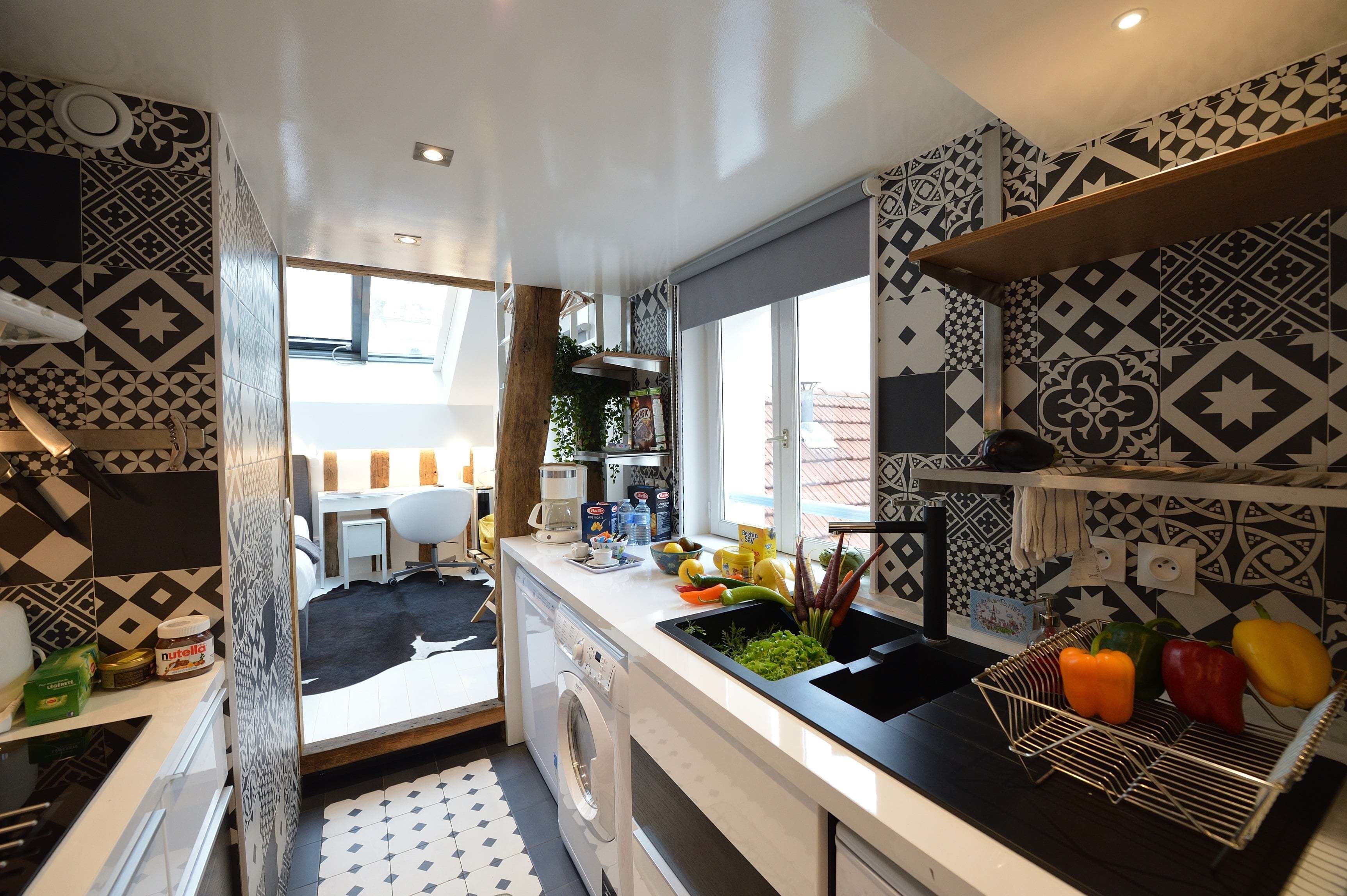 Cozinha moderna com azulejos estampados, máquina de lavar, pia com cesta de frutas e janela que ilumina naturalmente.