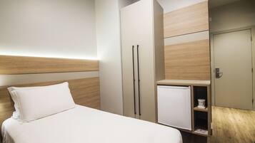 Quarto de hotel com cama, guarda-roupa e um pequeno frigorífico.