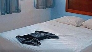 Quarto de hotel com cama, cabeceira de madeira e janela com cortinas.