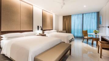 Quarto de hotel com duas camas, um banco, uma escrivaninha e uma cadeira.