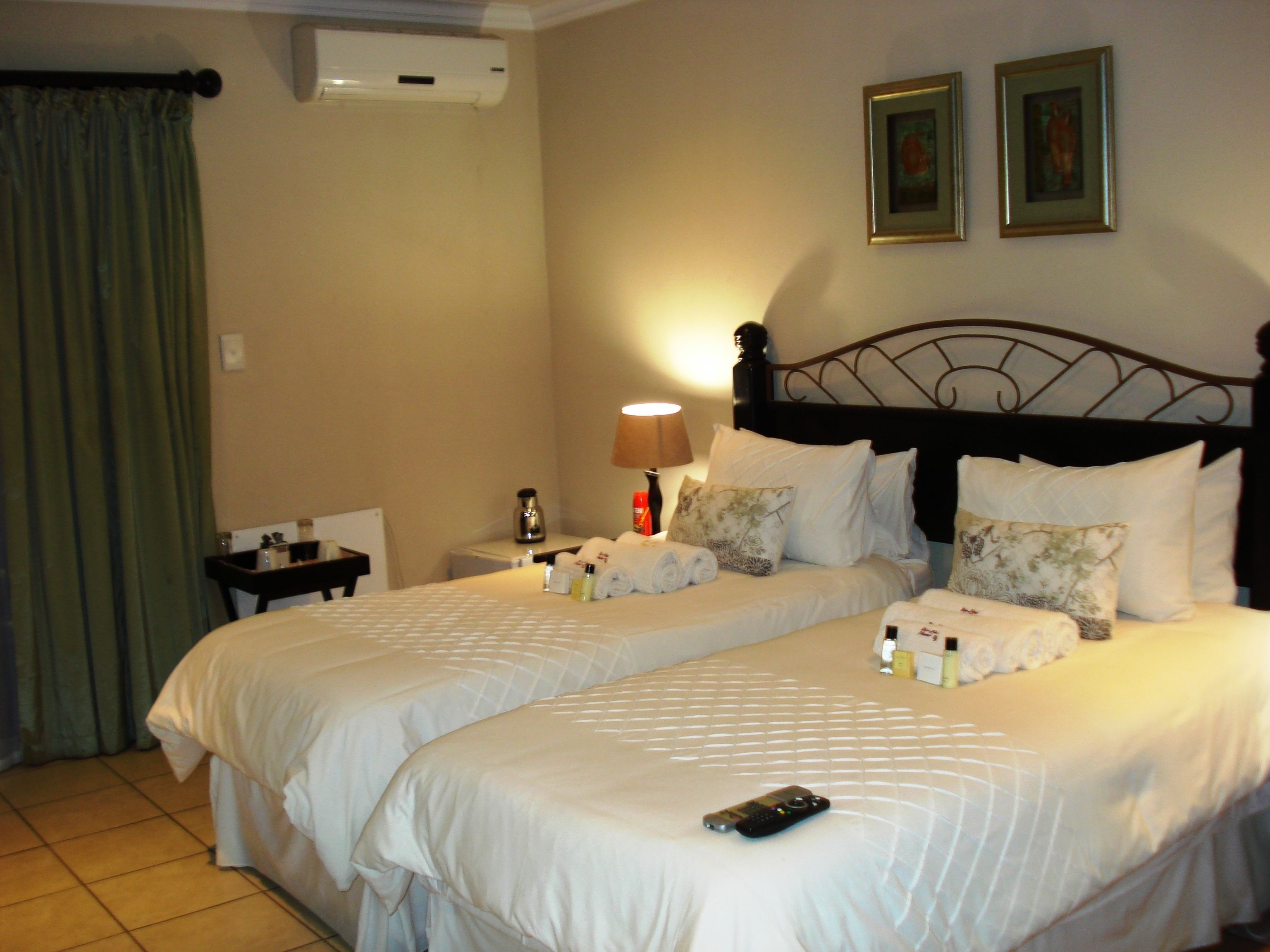 Quarto de hotel com duas camas, uma mesa de cabeceira, uma luminária e duas molduras na parede.