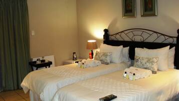 Quarto de hotel com duas camas, uma mesa de cabeceira, uma luminária e duas molduras na parede.