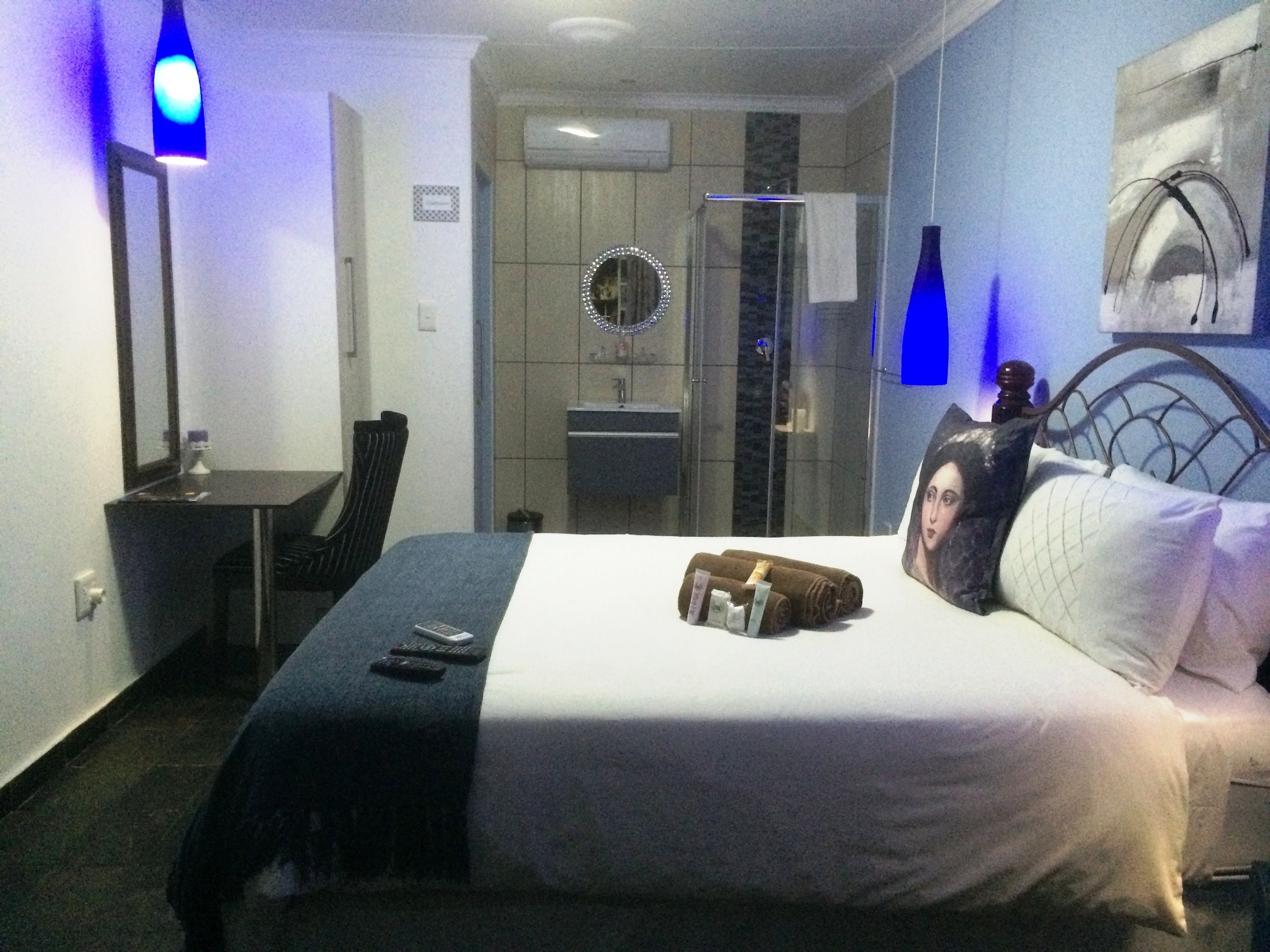 Quarto de hotel com cama, escrivaninha, cadeira, chuveiro e banheiro.