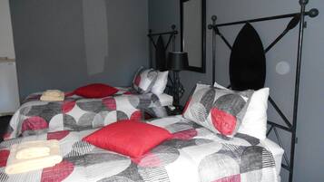 Cama bem arrumada com colcha estampada, um travesseiro vermelho e uma luminária preta ao lado.