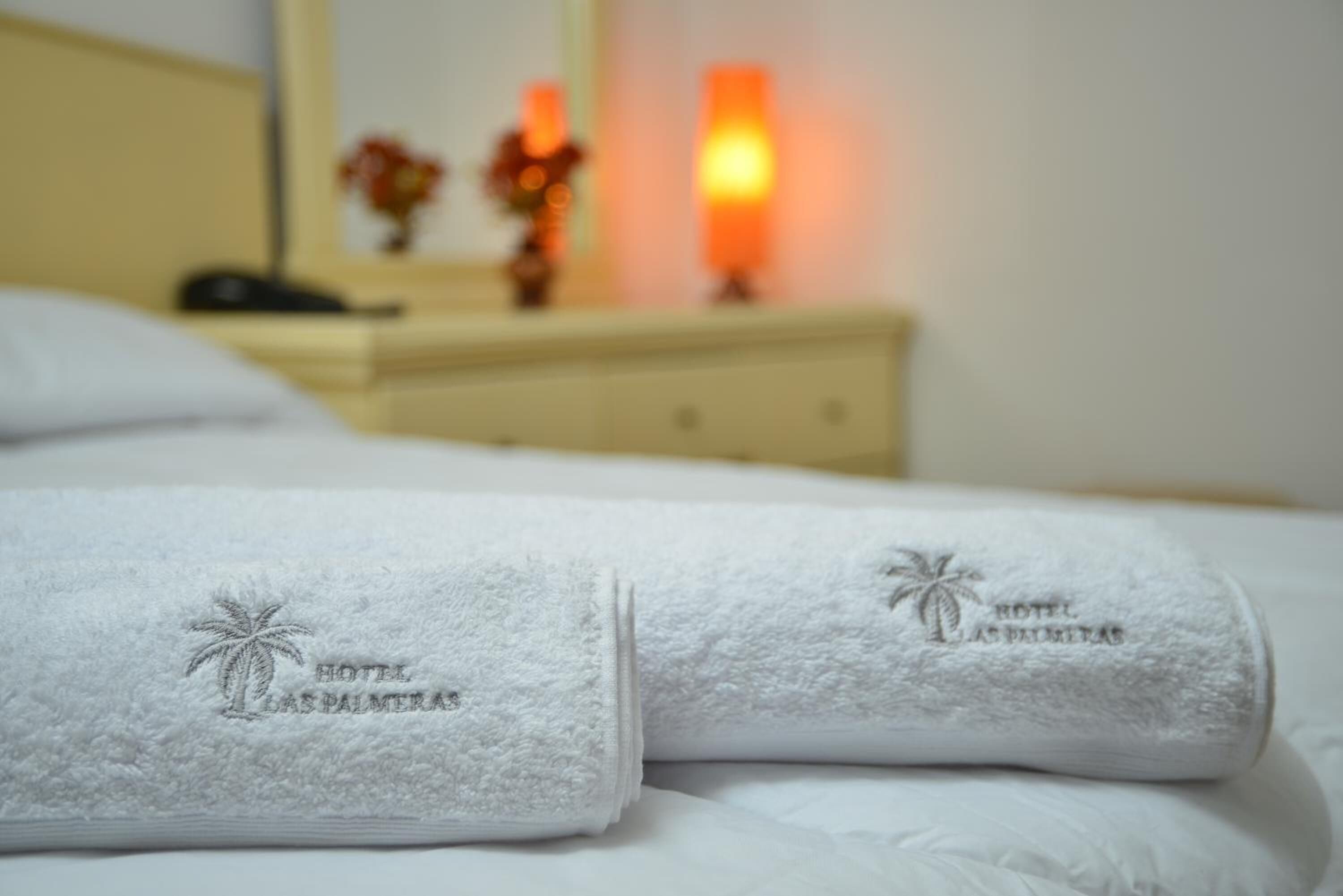 Cama bem arrumada com duas toalhas estampadas com palmeira e nome do hotel.