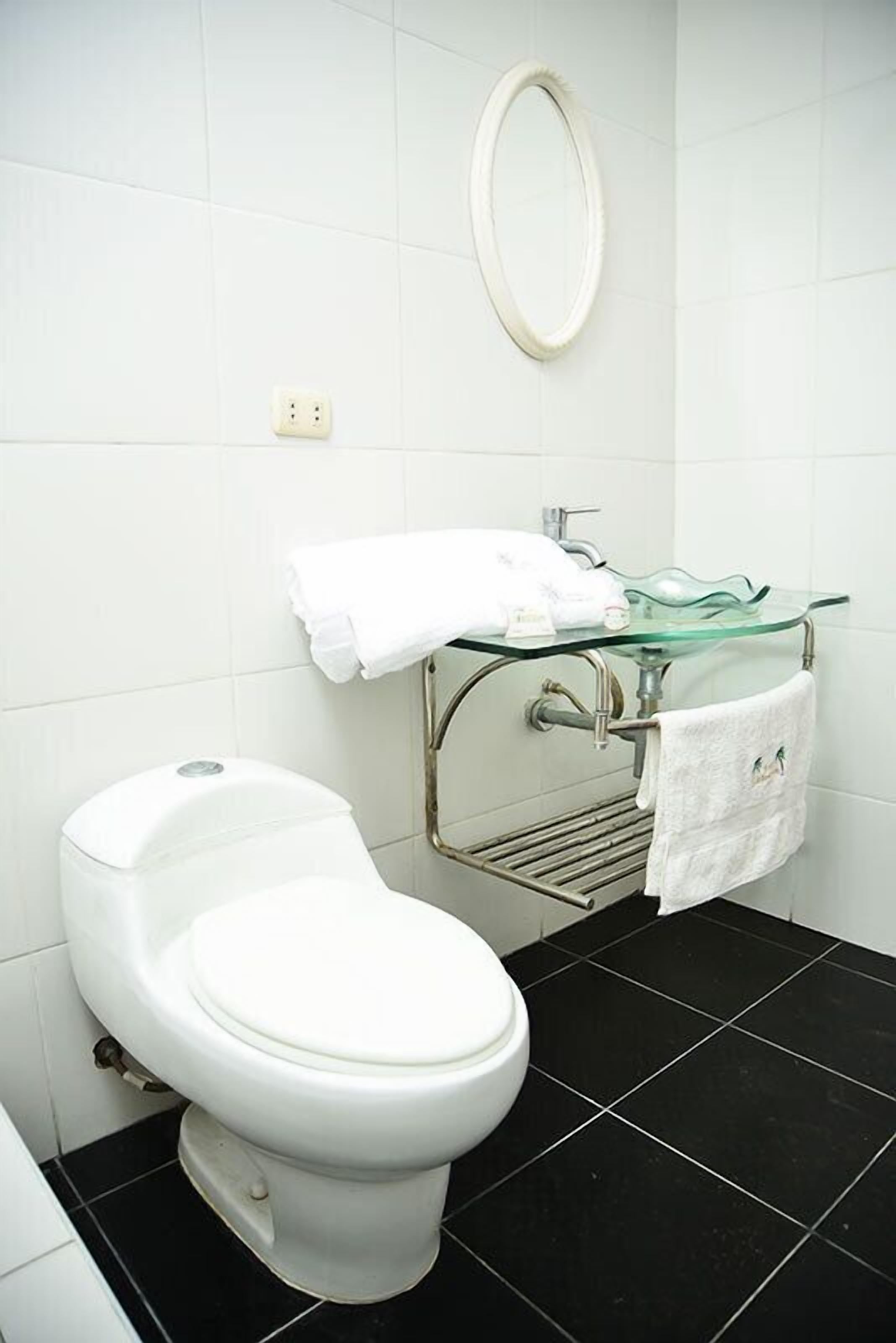 Um banheiro com vaso sanitário branco, pia de vidro e uma toalha branca pendurada na parede.