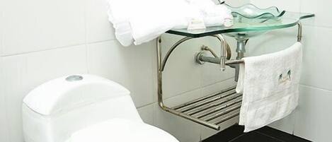 Um banheiro com vaso sanitário branco, pia de vidro e uma toalha branca pendurada na parede.
