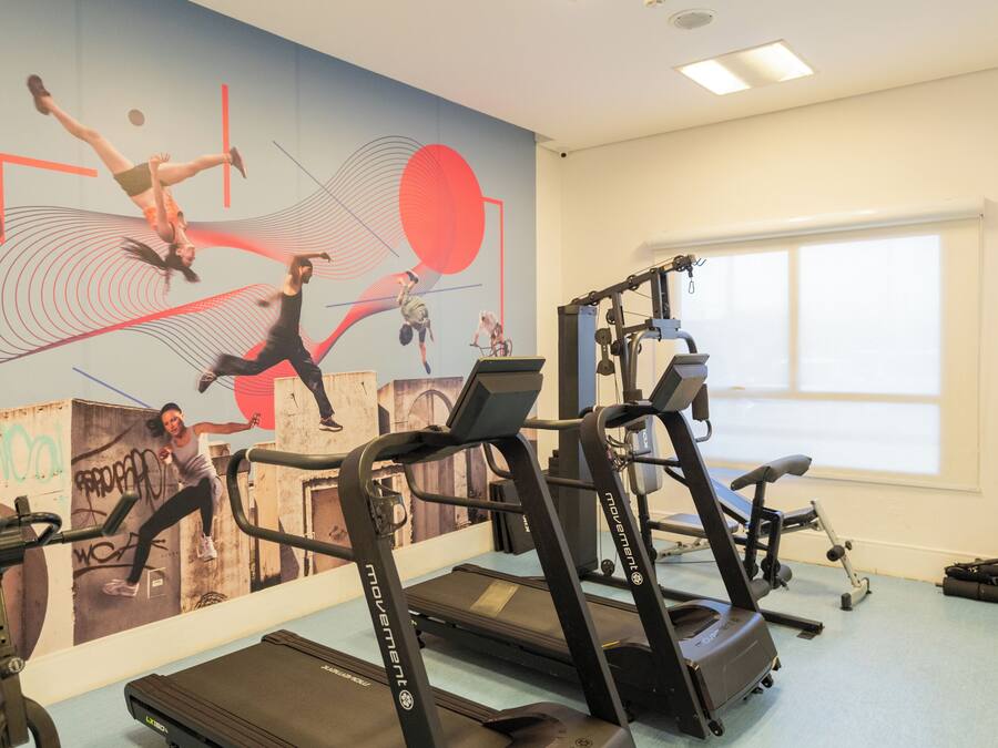 Uma academia com equipamentos de exercício, um mural e uma janela.