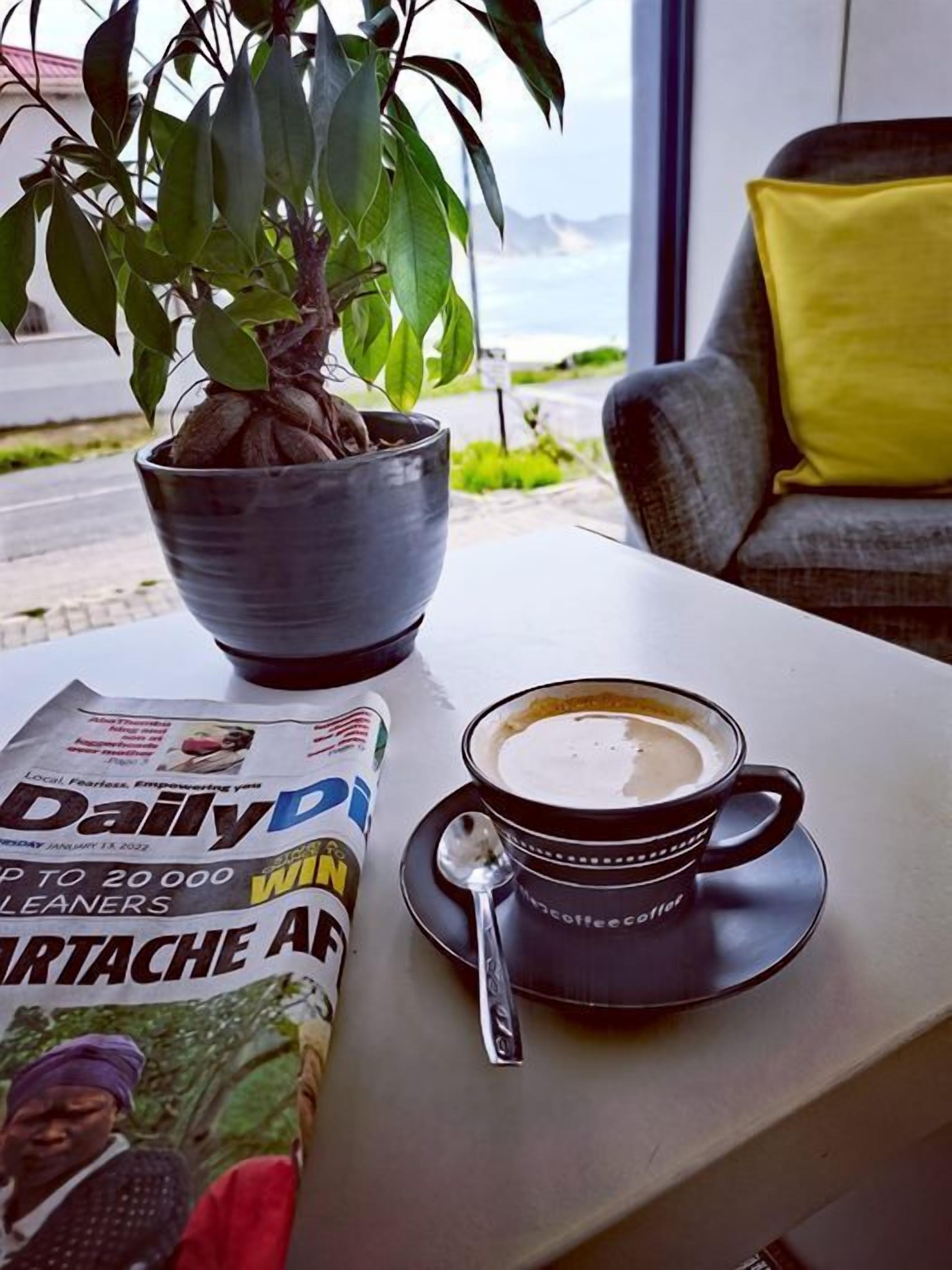 Um jornal, uma chávena de café e uma planta em vaso sobre uma mesa.