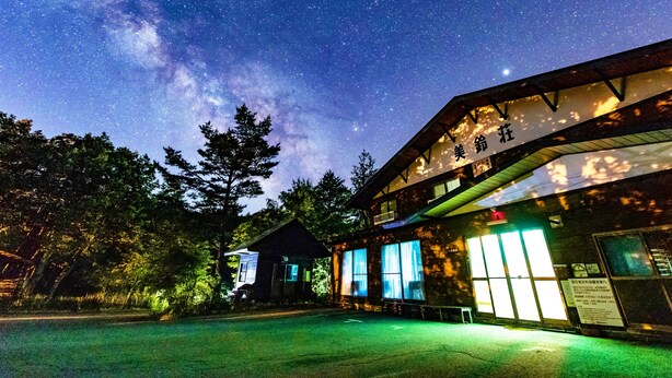 Um edifício com céu estrelado, uma construção menor adjacente e uma entrada bem iluminada.