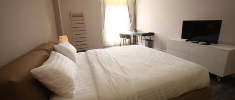 Quarto de hotel moderno com uma cama grande, uma mesa de escritório, uma televisão e uma janela com cortinas.