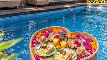 Bandeja flutuante em formato de coração com itens de café da manhã e bebidas em uma piscina.