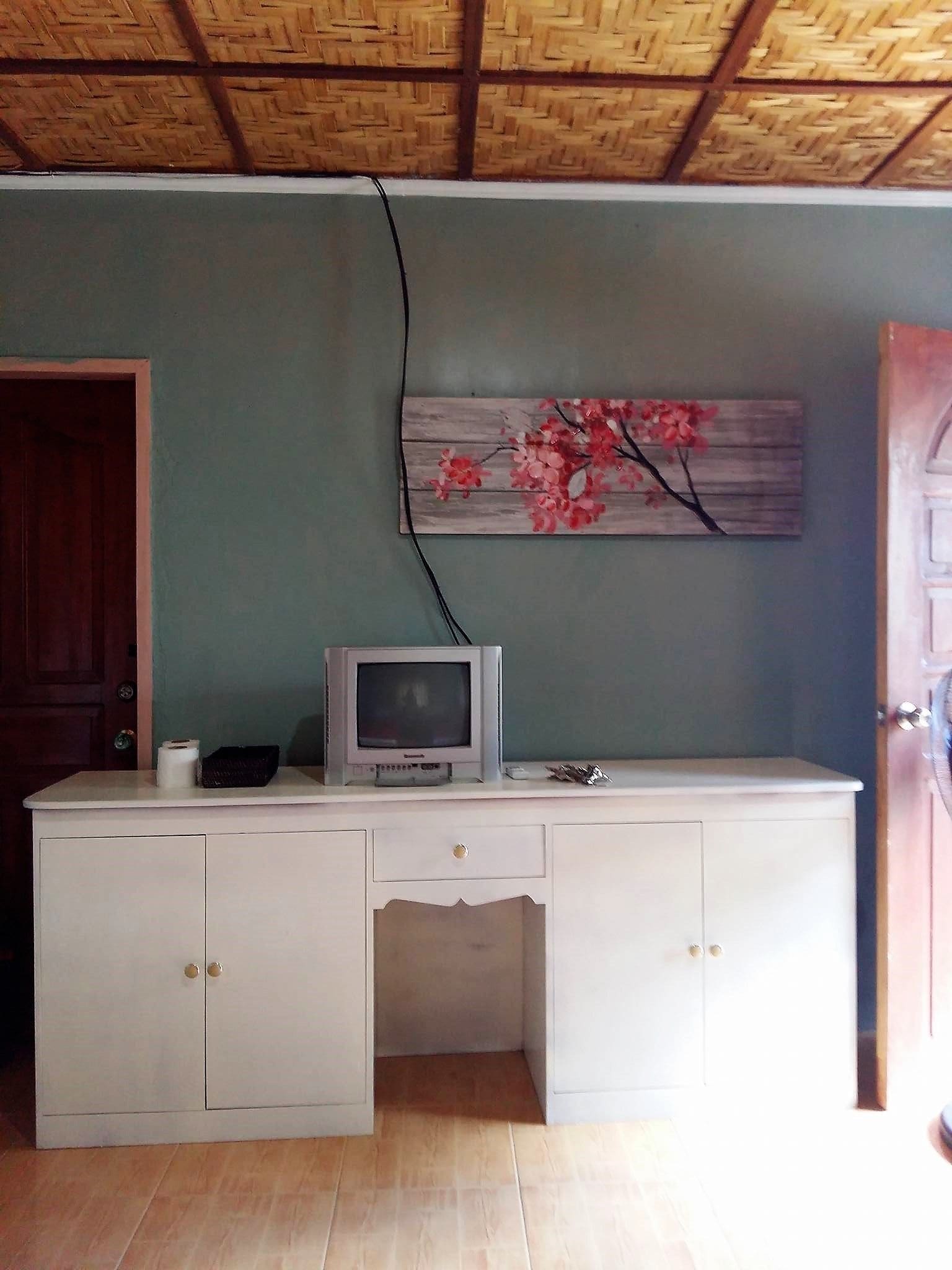 Quarto com teto de madeira, escrivaninha com televisão e pintura pendurada na parede.