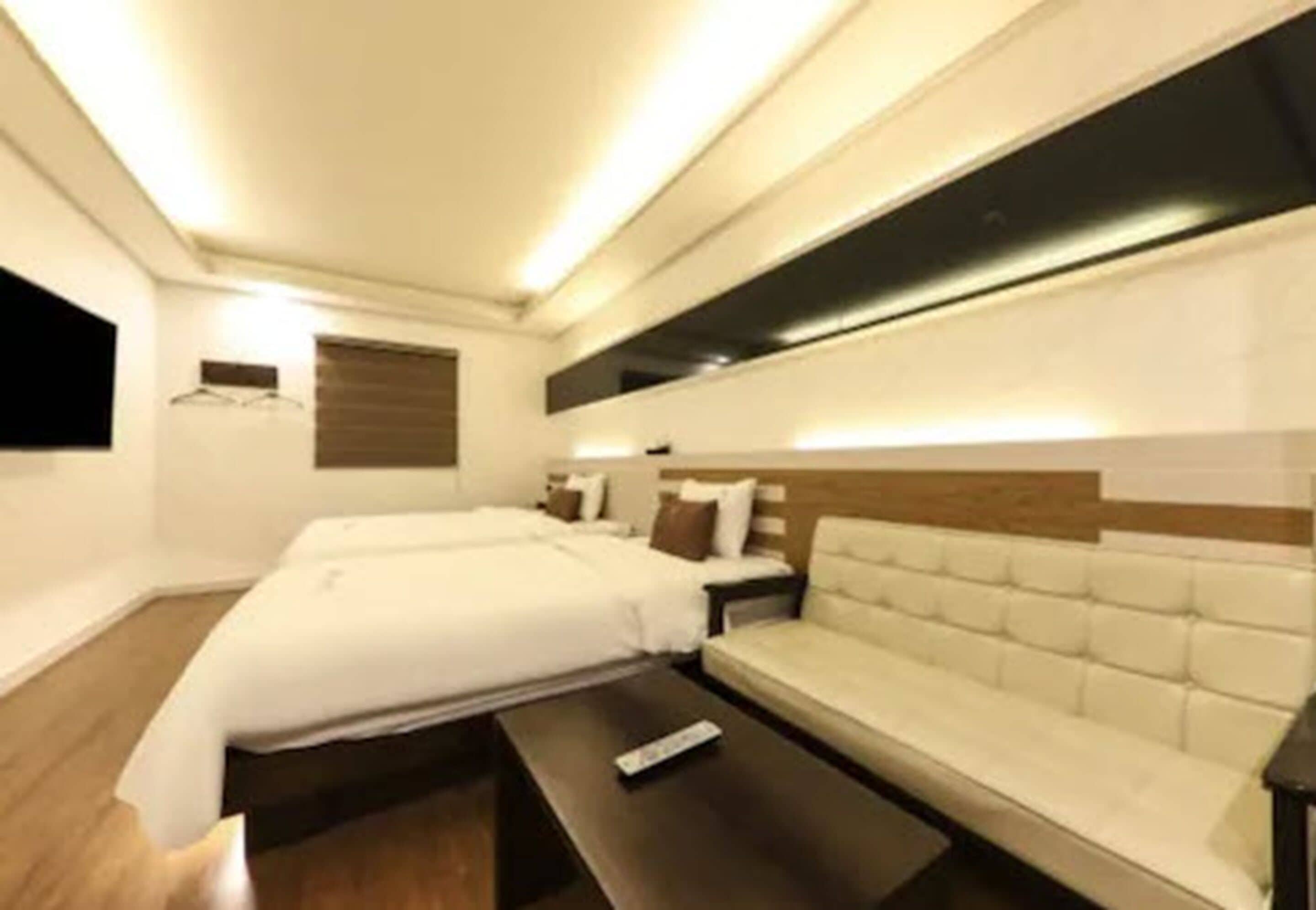 Quarto de hotel com cama, sofá, mesa pequena e televisão presa na parede.