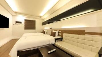 Quarto de hotel com cama, sofá, mesa pequena e televisão presa na parede.