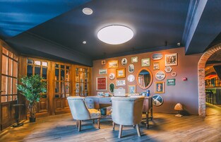 Um quarto aconchegante com uma escrivaninha de madeira, cadeiras e uma parede decorada com diversas fotos emolduradas.