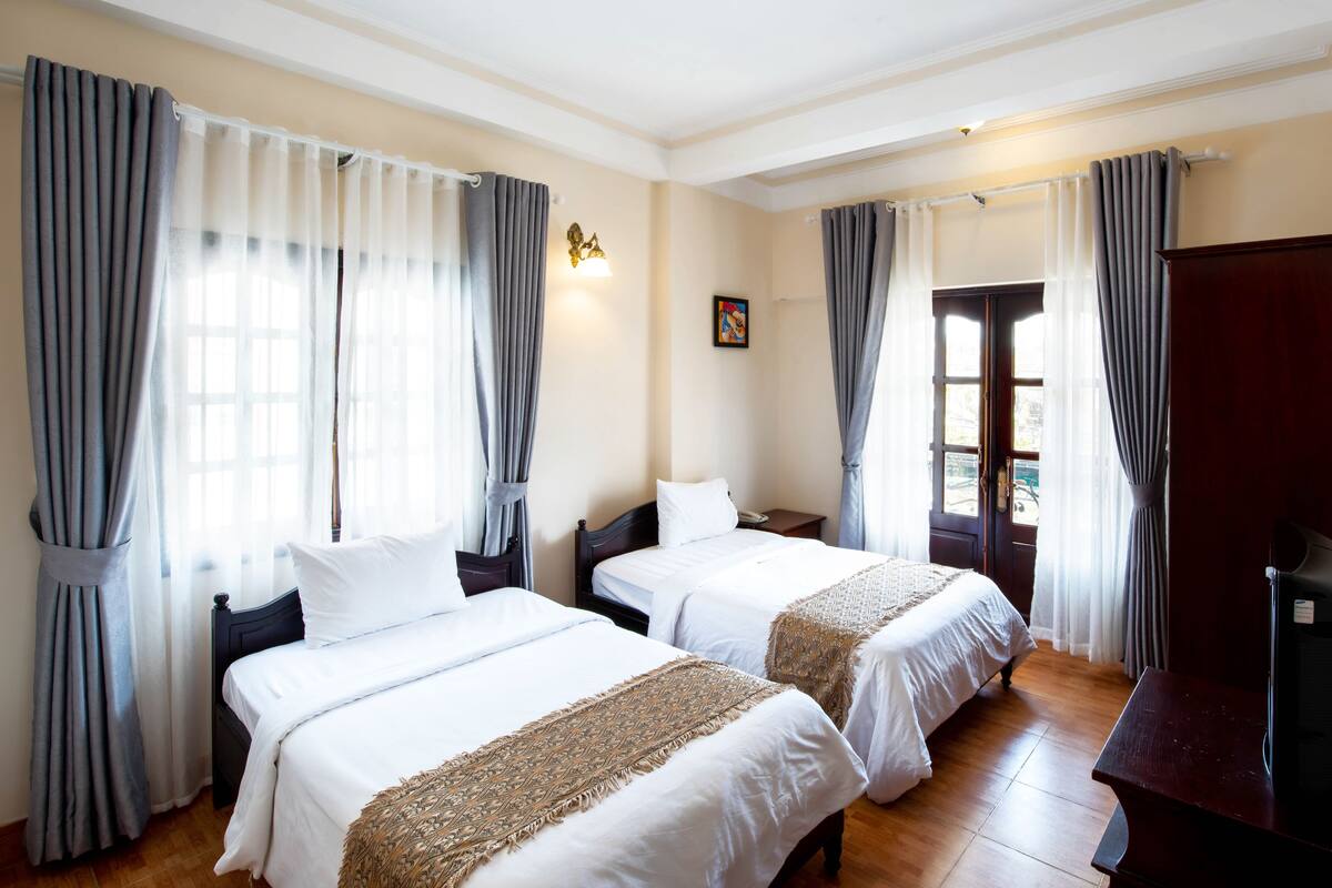 Quarto de hotel com duas camas, televisão e janela com cortinas.