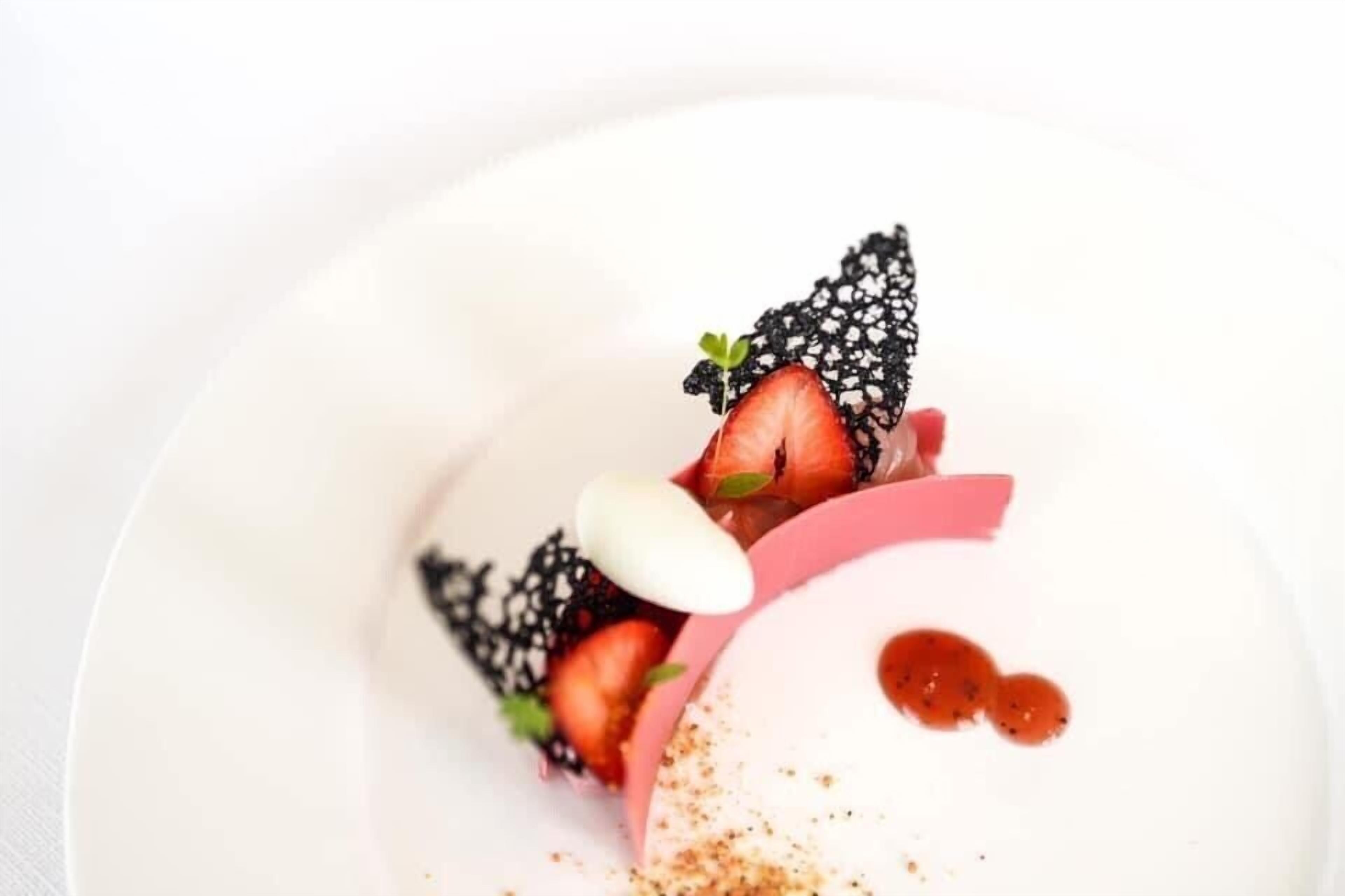 Sobremesa com morangos, chocolate e uma colherada de creme em um prato branco.