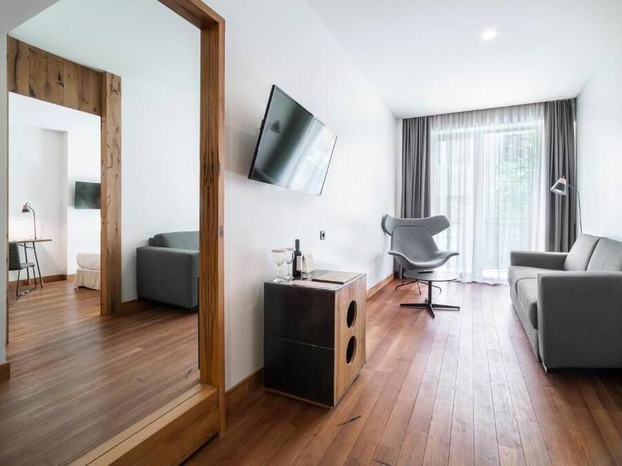 Uma sala de estar moderna com uma TV de tela plana na parede, um sofá cinza, uma mesa de centro preta e piso de madeira.