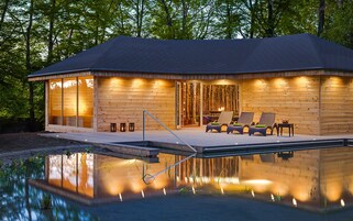 Uma cabana moderna de madeira com piscina, apresentando um deck com espreguiçadeiras e área de refeições.