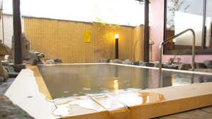 Uma piscina de águas termais com um deque de madeira, uma parede de pedra e um poste de luz.